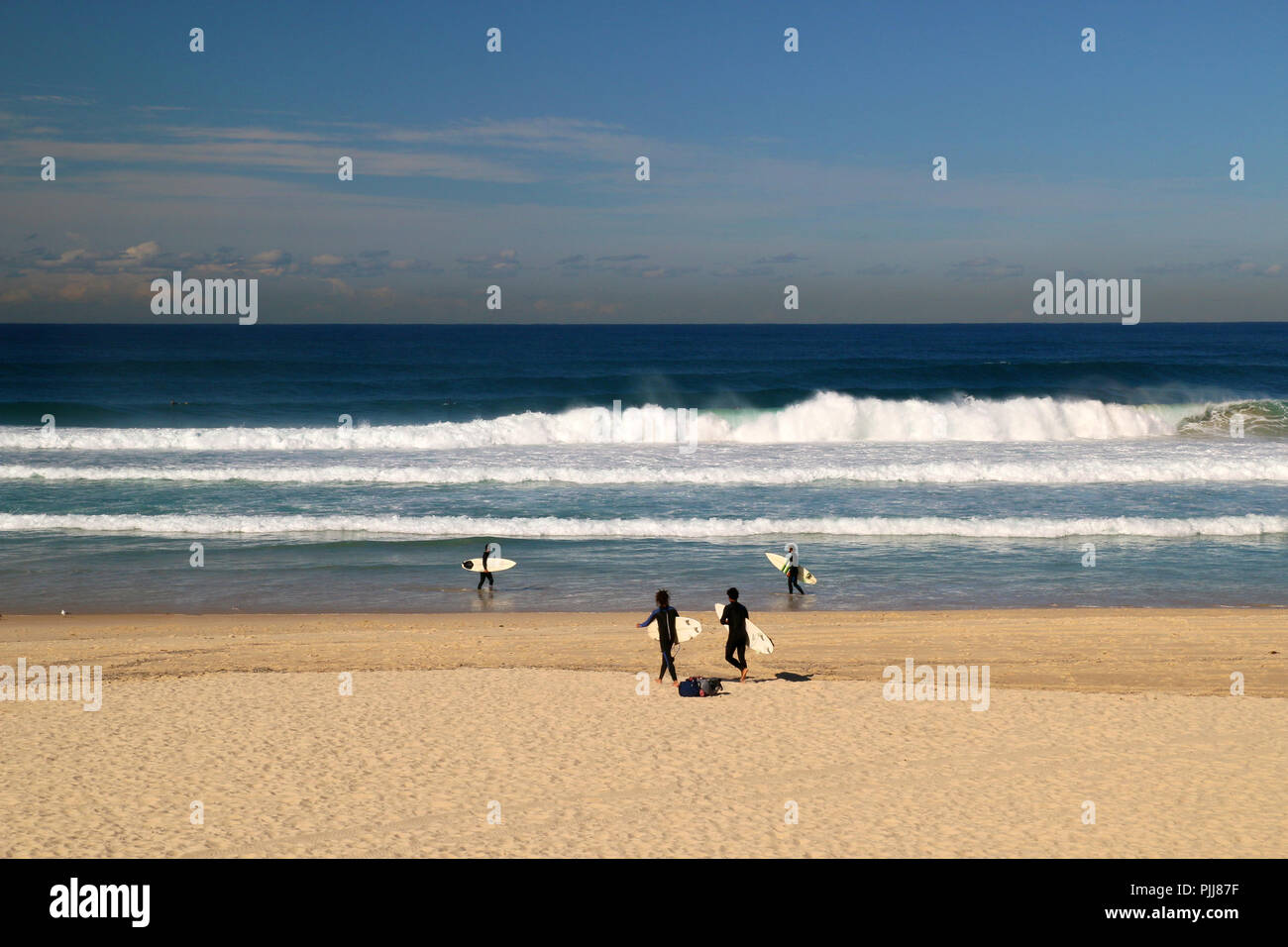Deep blue Pacific ocean beach scene with huge waves and surfers walking ...