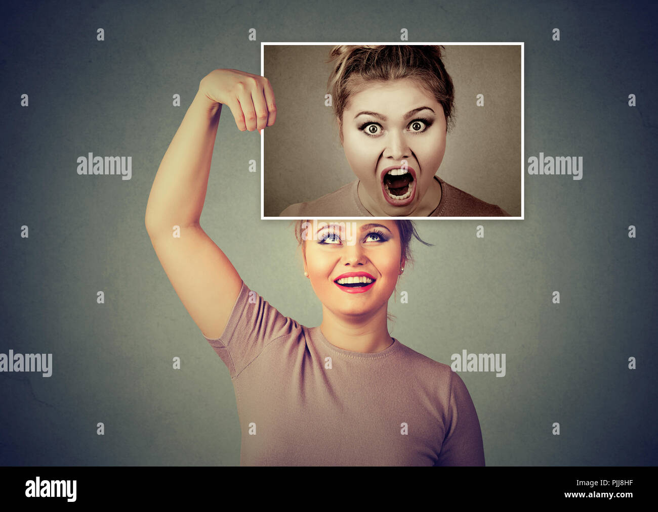 Young woman smiling while holding picture of herself in angry mood and ...