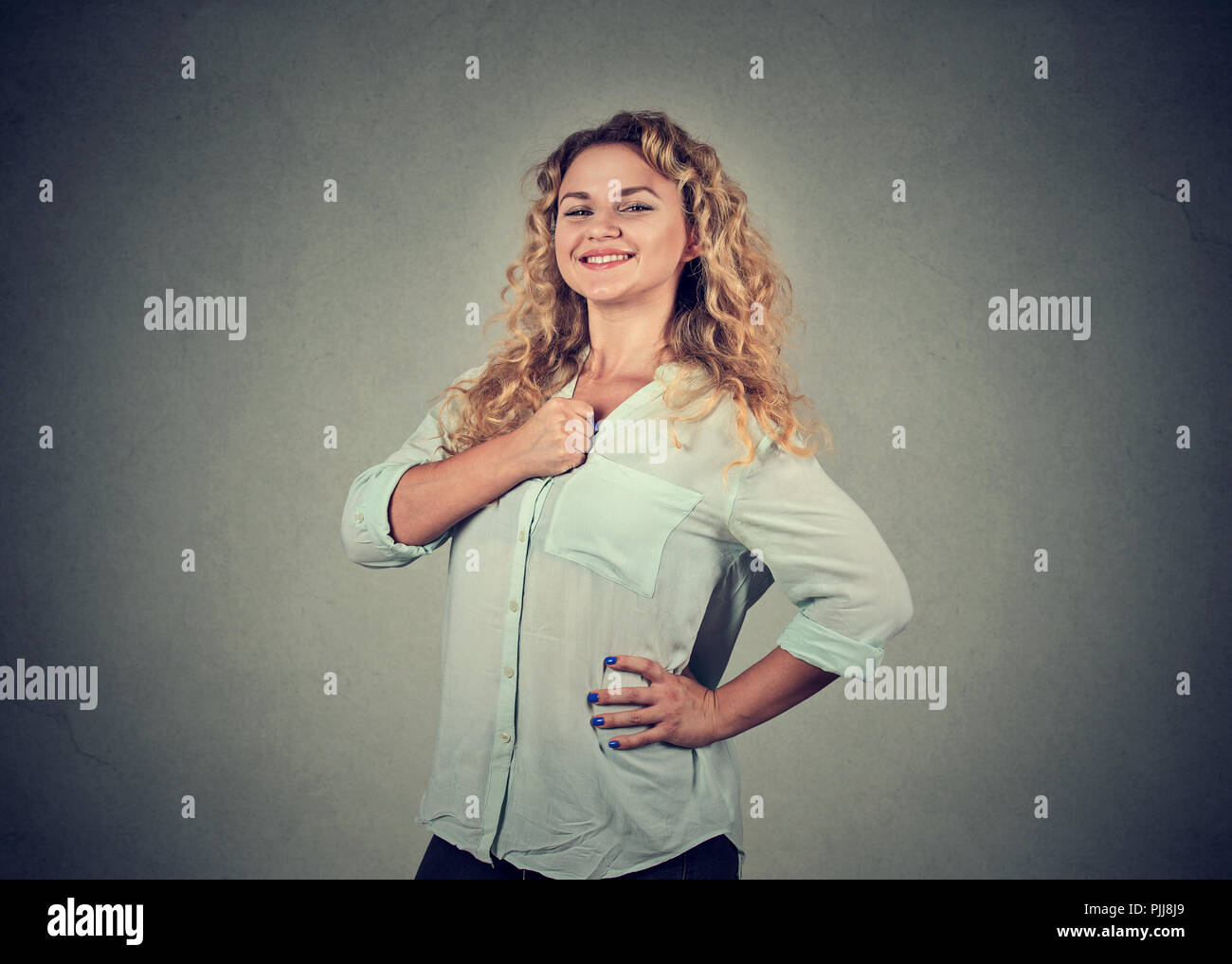Modern young woman holding hand on chest in pride standing on gray ...