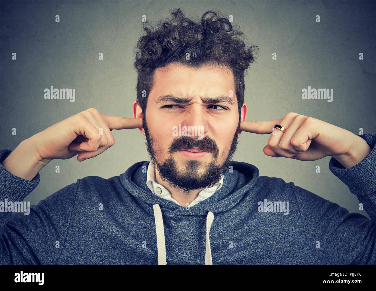 Closeup portrait of a displeased man plugging ears with fingers doesn't ...