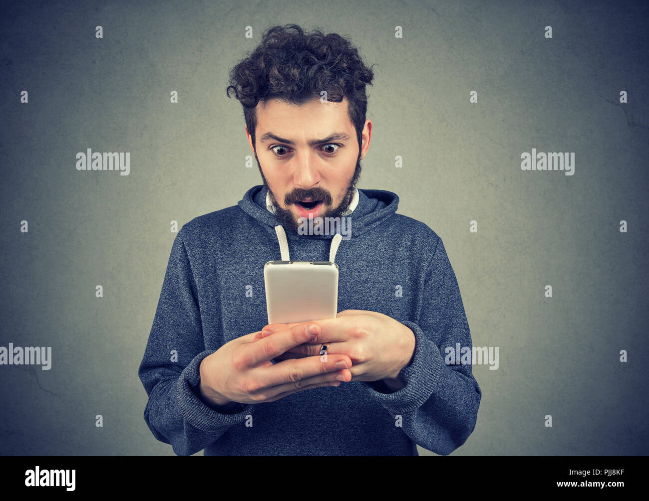 Portrait of an anxious young man looking at phone seeing bad news or ...