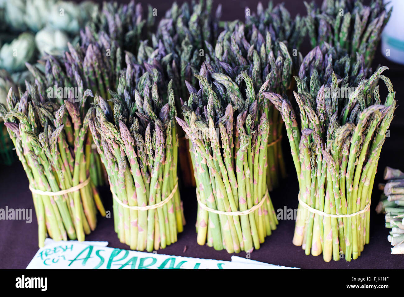 Frontal view of asparagus stalks in a bunch at a farmers market stall ...