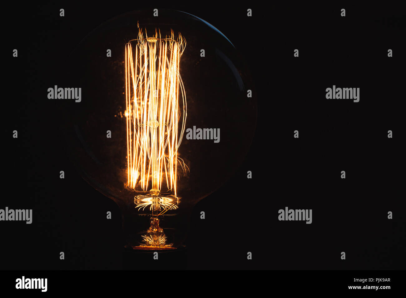 Vintage stylized large tungsten lamp glowing over dark background ...