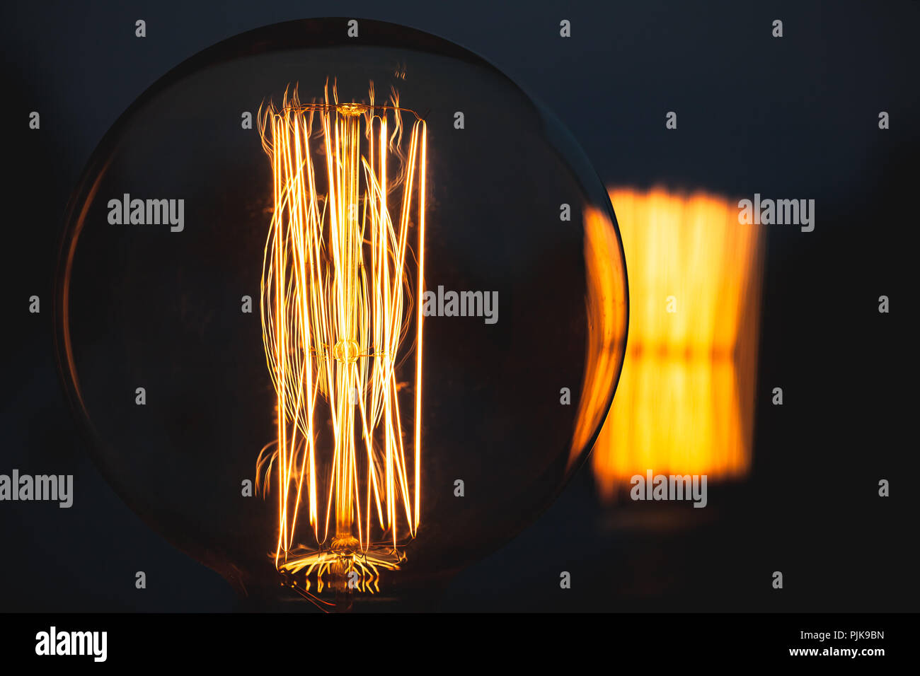 Retro stylized large tungsten lamp glowing over dark background, close ...