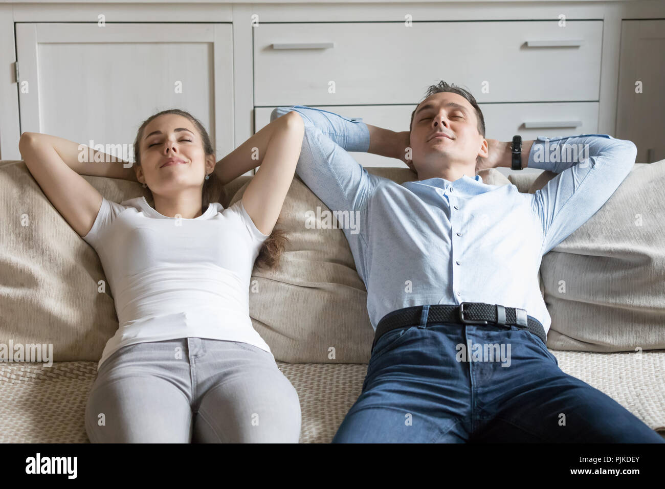Tired man and woman relaxing on sofa hands over head Stock Photo - Alamy