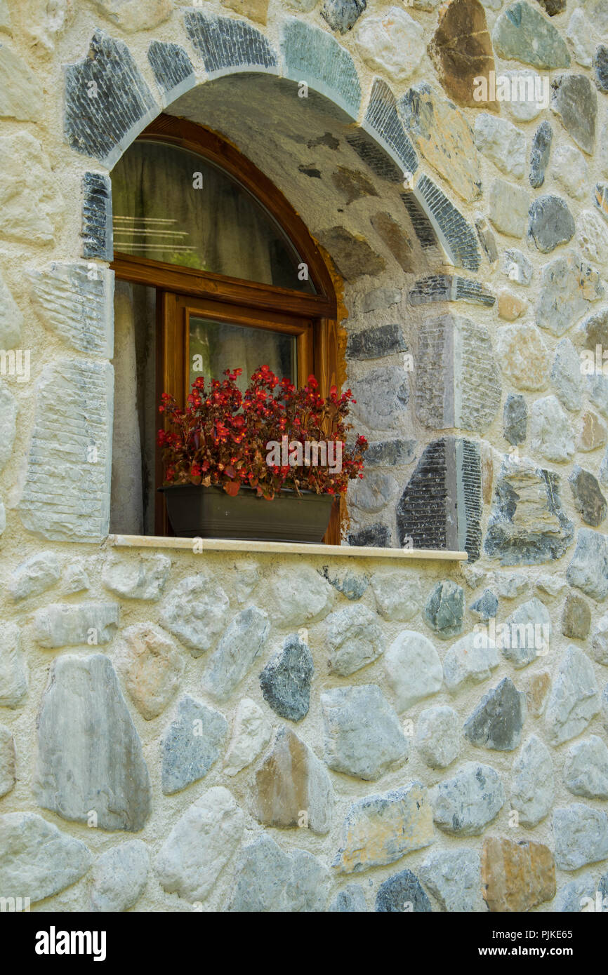 Detail of a stone house facade with arched window and flowers on the ...