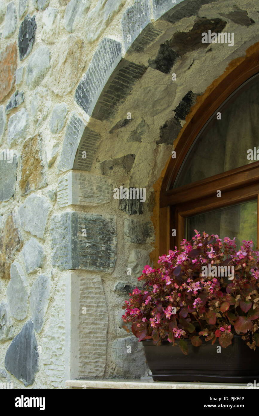 Detail of a stone house facade with arched window and flowers on the ...