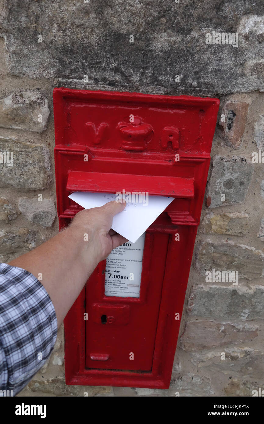 Mans hand posting letter into an English village post box that is built ...