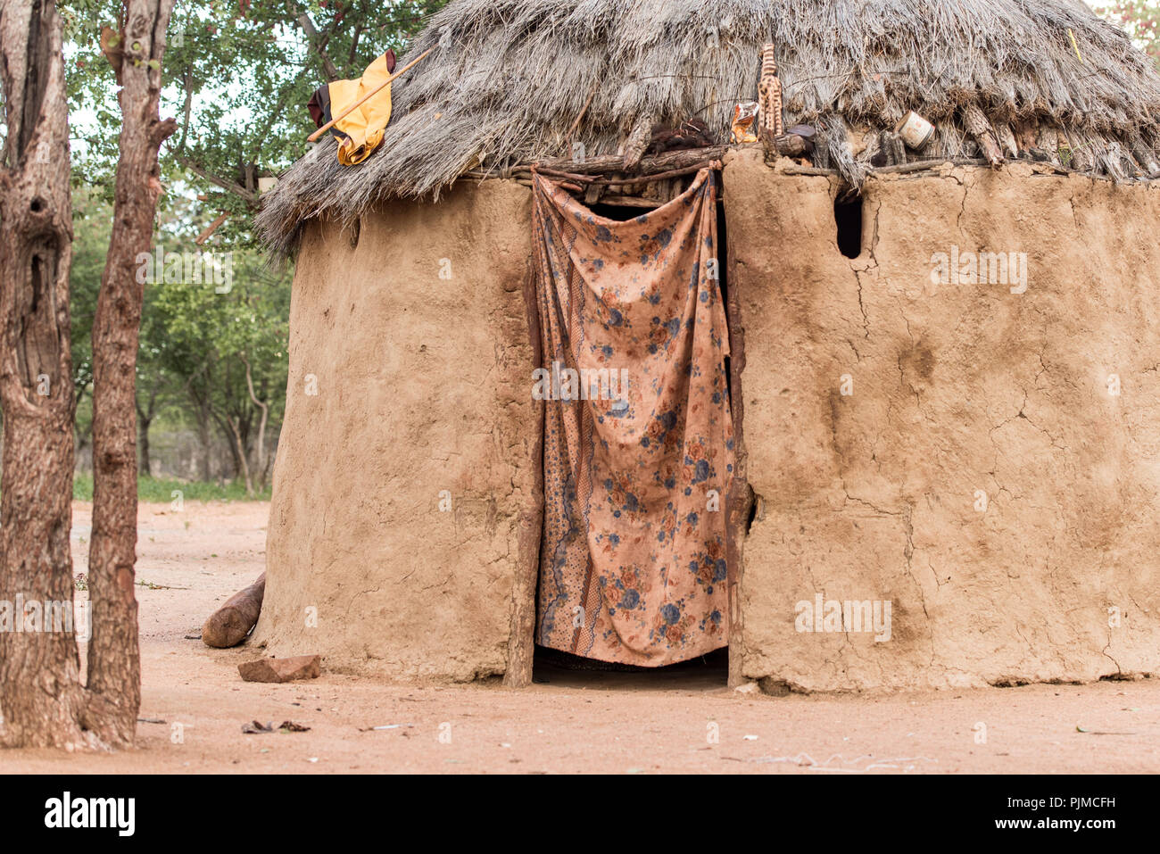 Mud hut with thatched roof and curtain in front of the door opening in ...