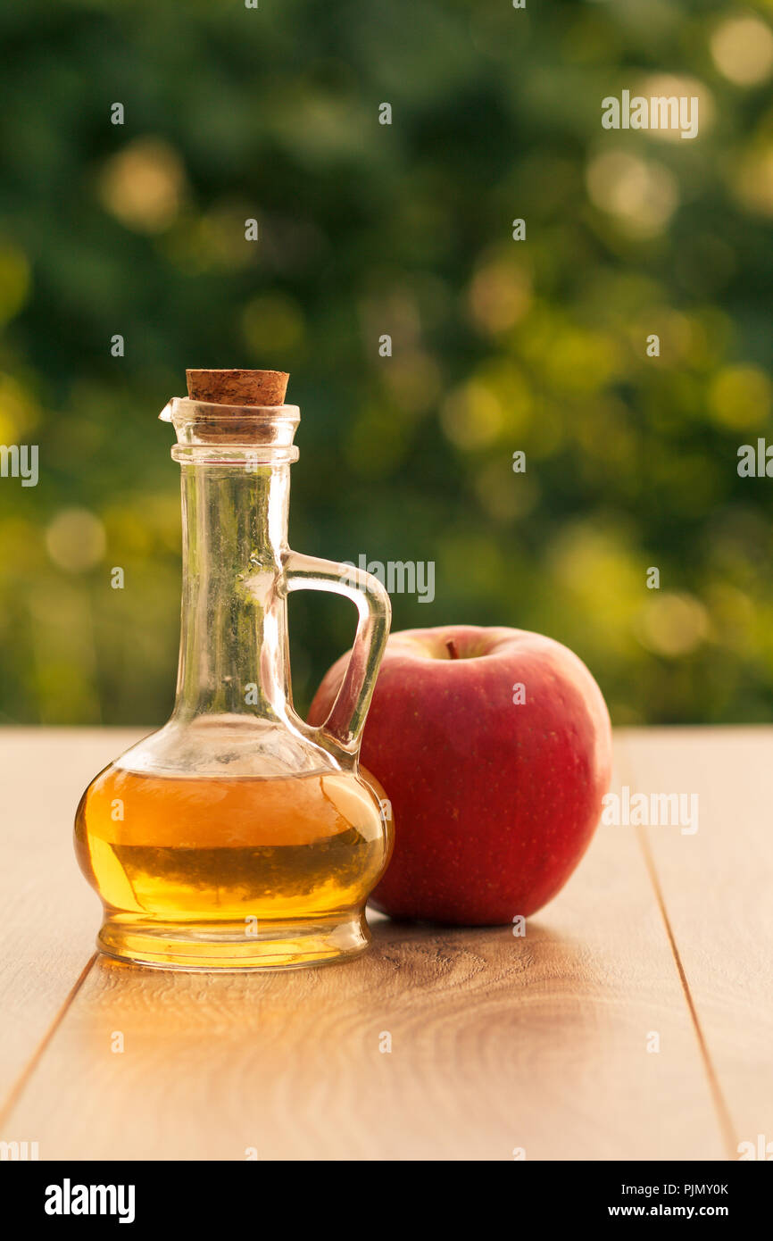 Apple vinegar in glass bottle with cork and fresh red apple on wooden ...