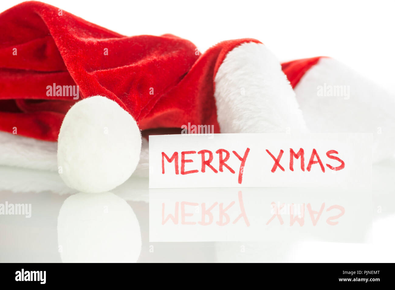 White card with merry xmas sign leaning on santa hat. On a white table ...