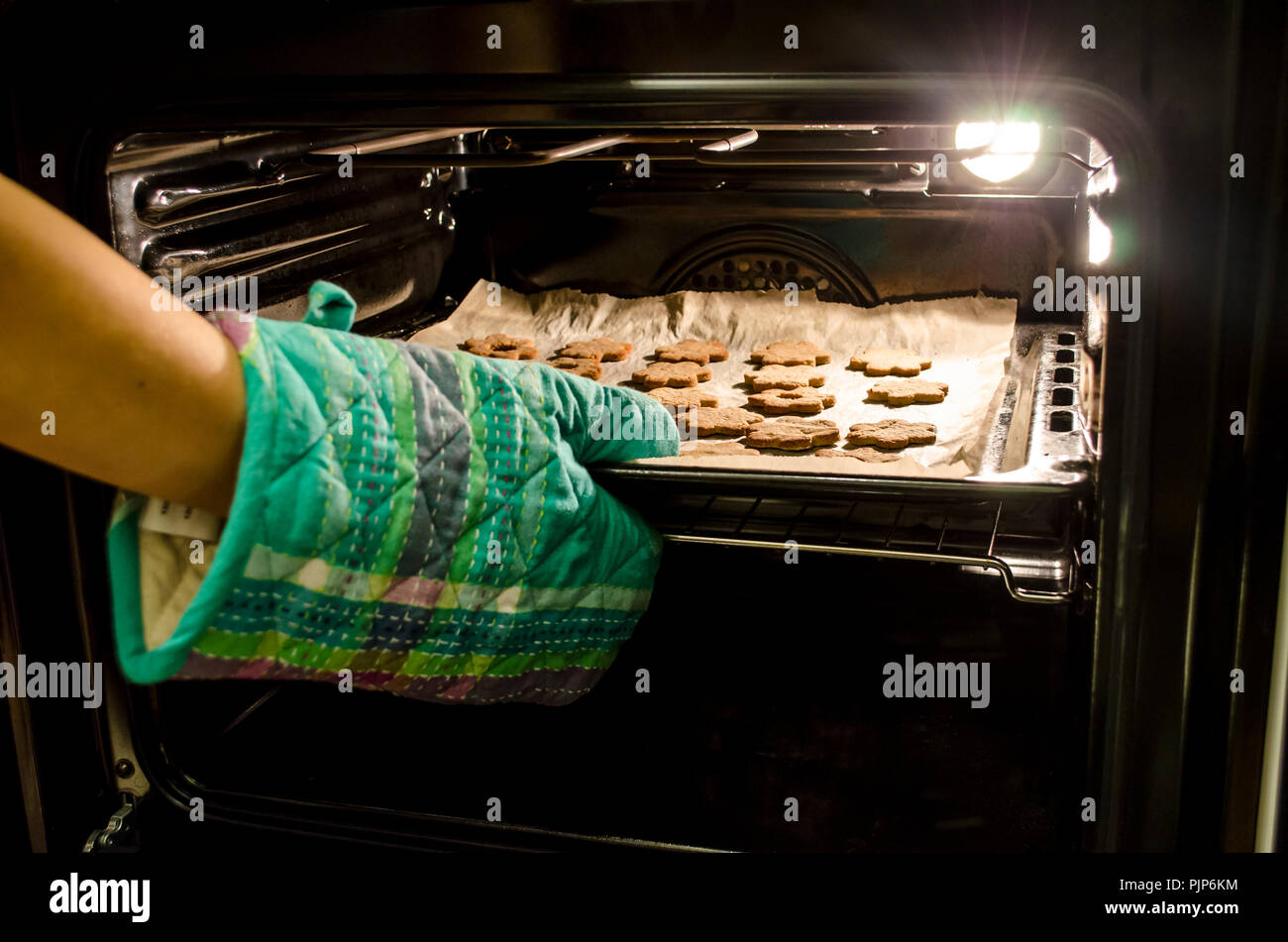 Taking baked cookies out of the oven with kitchen gloves Stock Photo ...