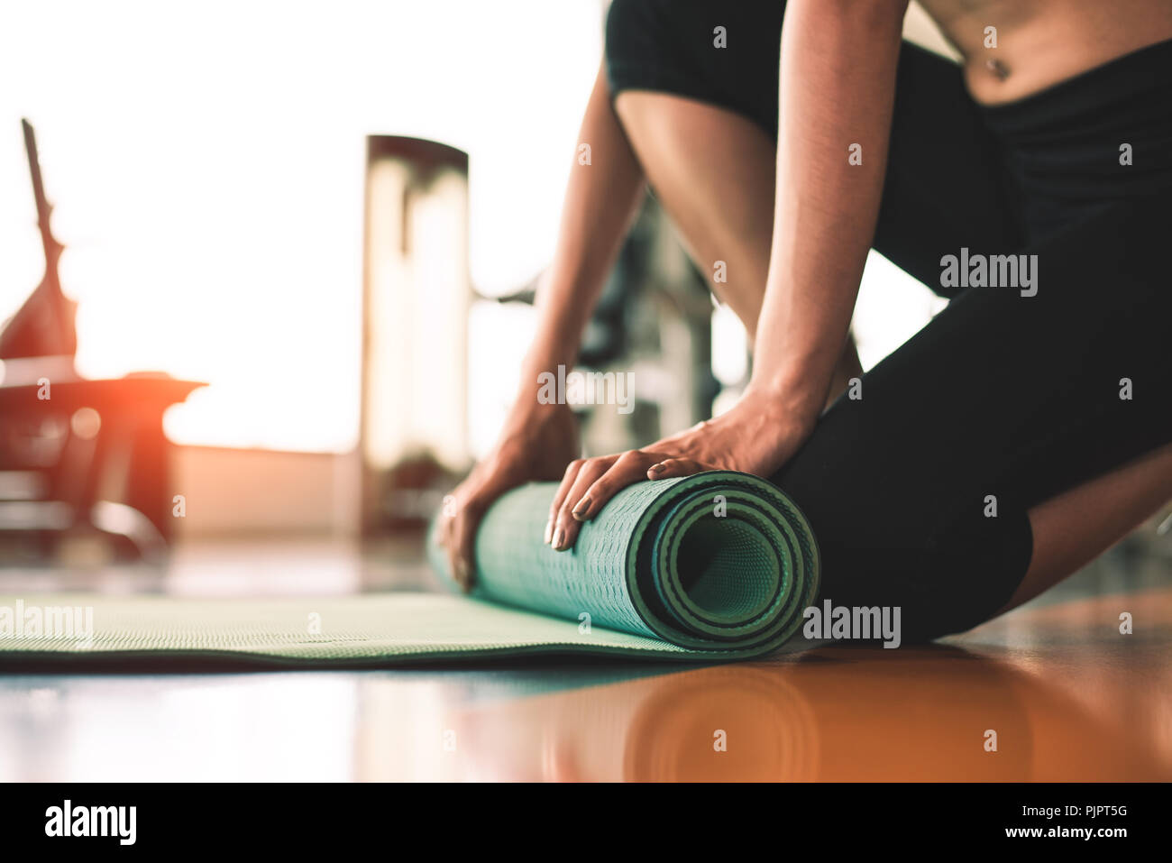 Close up of sporty woman folding yoga mattress in sport fitness gym ...