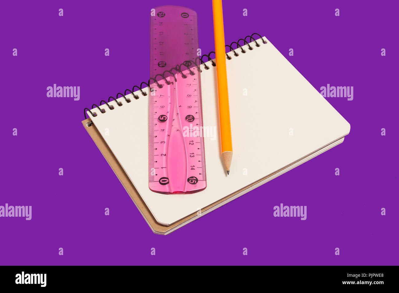 spiral opened notebook with pencil and ruler lying on a purple ...