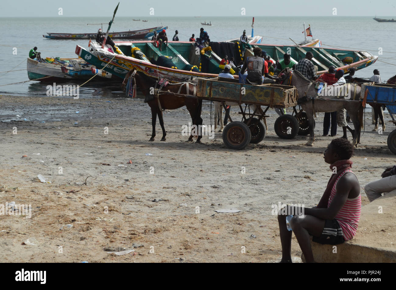 A crowded beach in Mbour, Senegal, with fishers landing their catch and ...