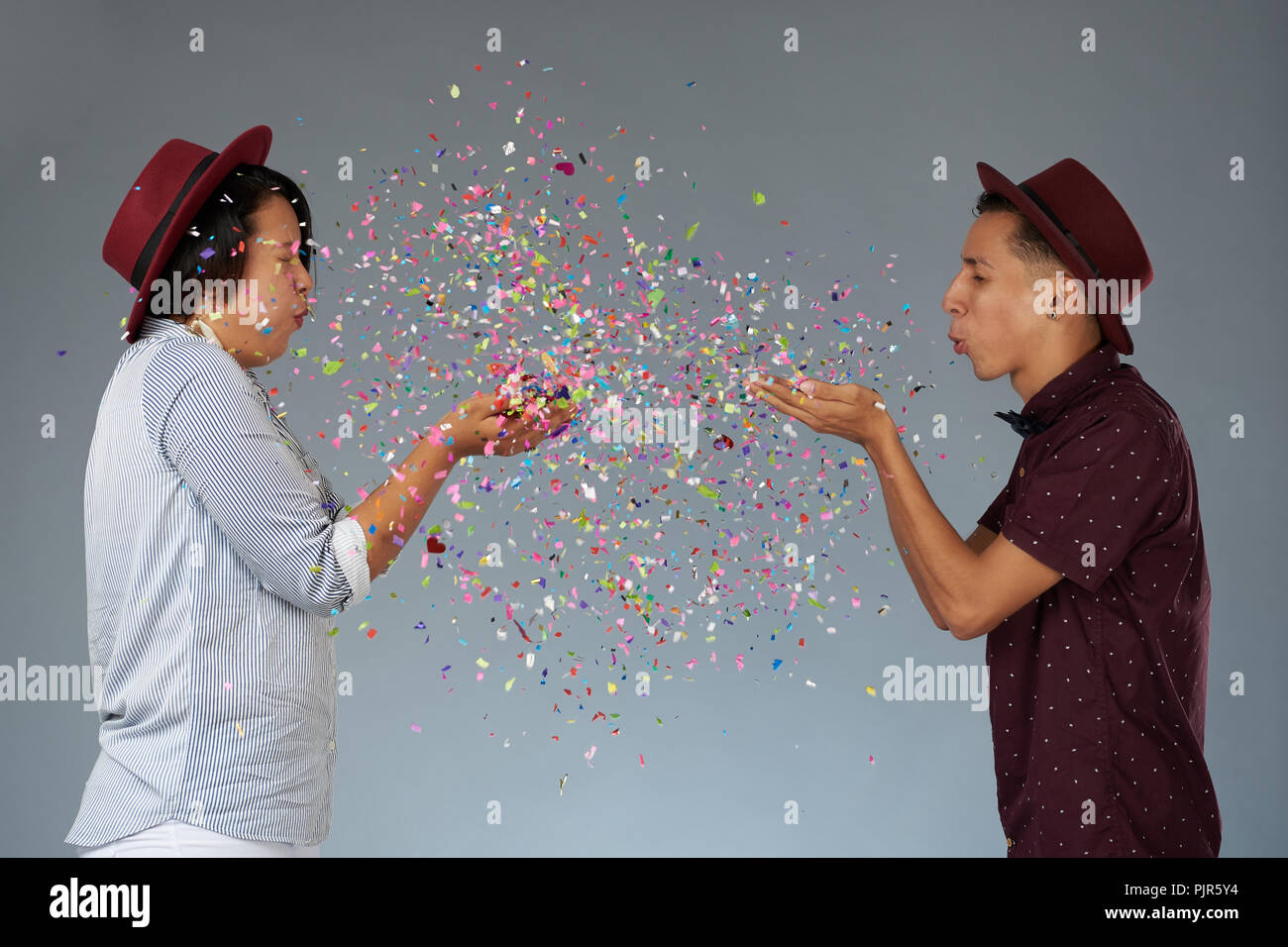 Two people blow confetti on gray studio background Stock Photo - Alamy