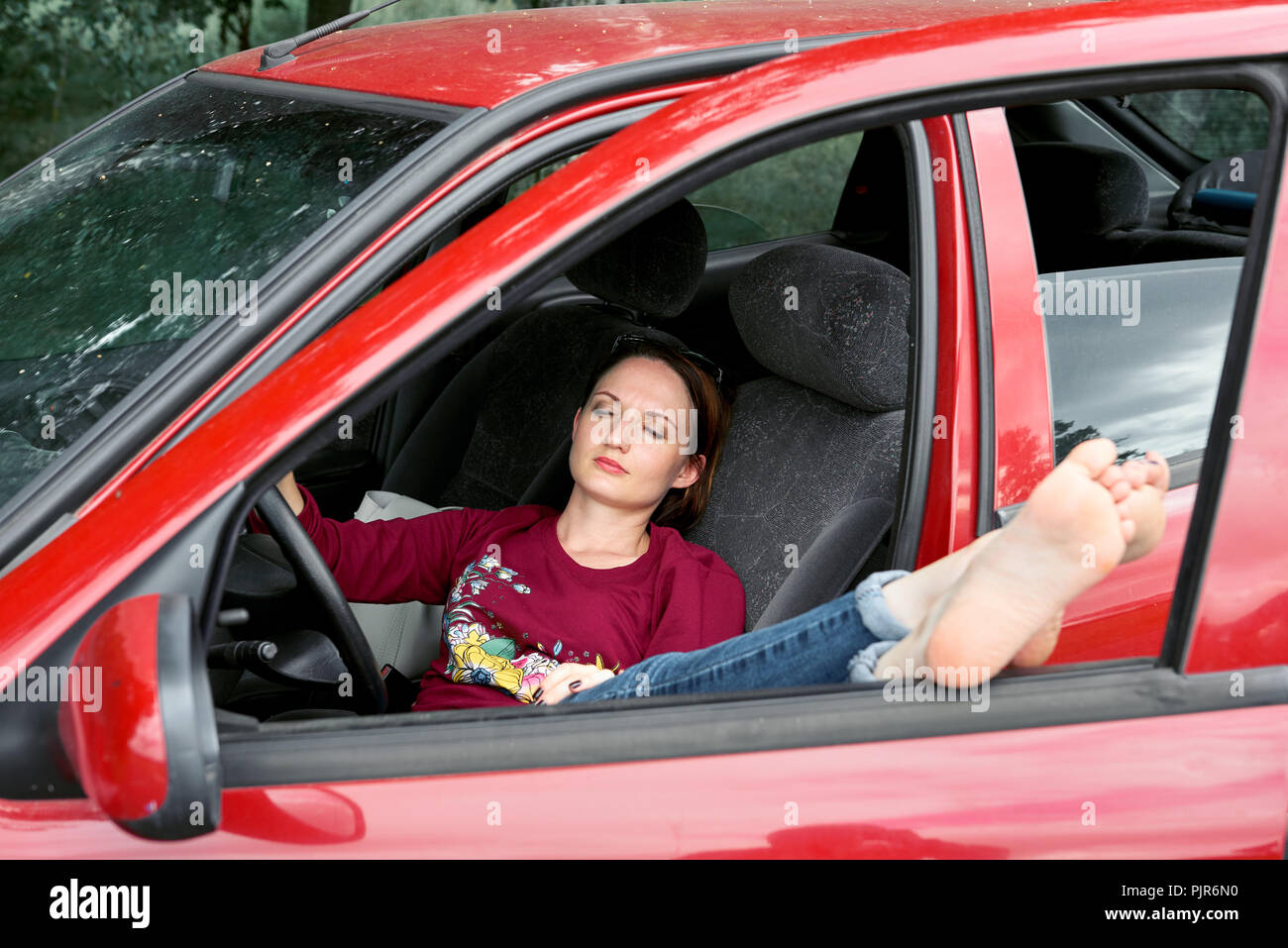 young woman driver resting in a red car, put her feet on the car window ...