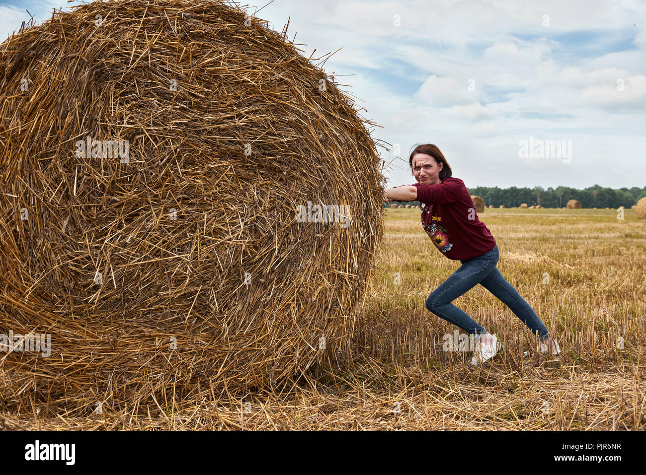 young girl having fun in the field, pushes the haystack Stock Photo - Alamy