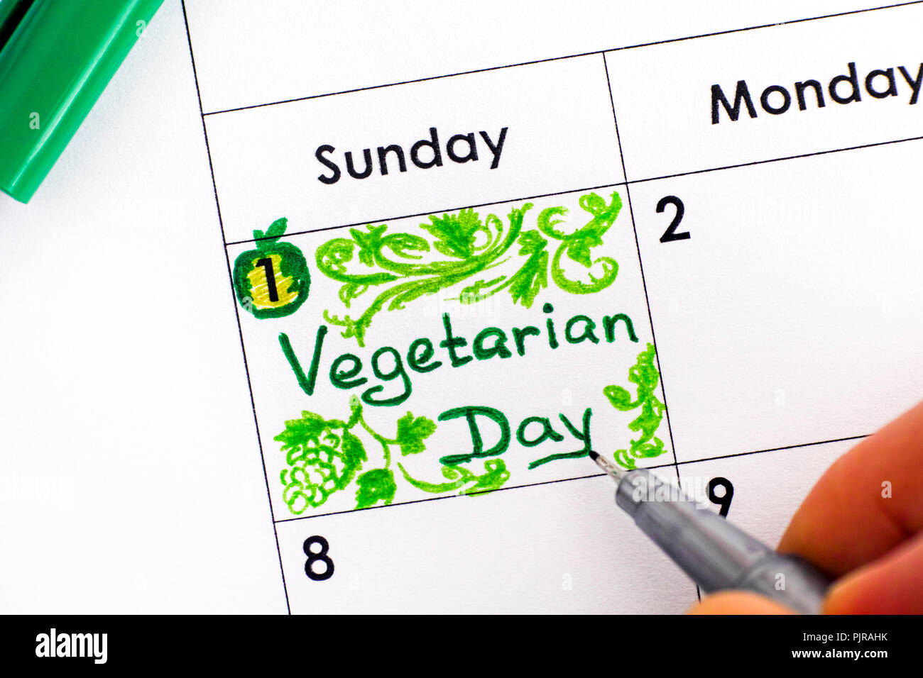 Woman fingers with pen writing reminder Vegetarian Day in calendar ...