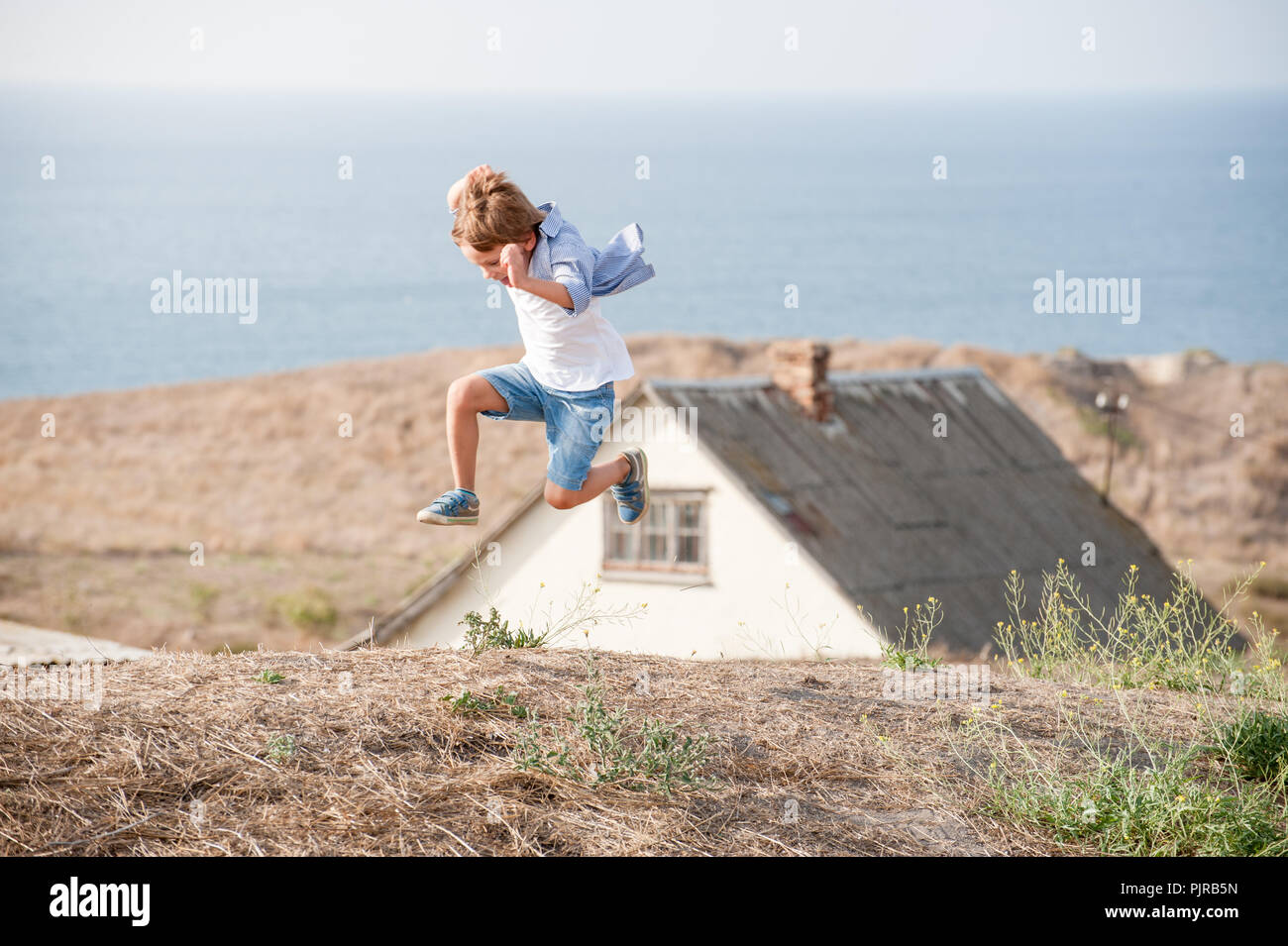 healthy active caucasian kid jumping high on hill on old house and sea ...