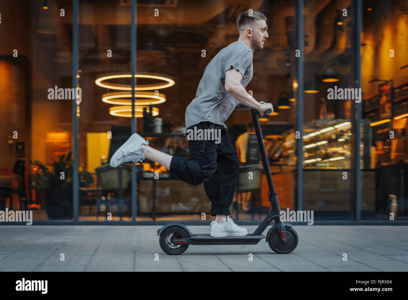 Attractive man riding a kick scooter at cityscape background Stock ...