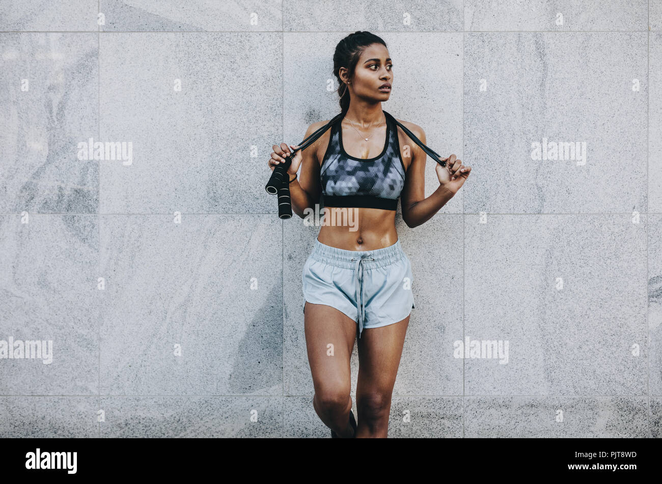 fitness woman relaxing outdoors standing against a wall while training ...