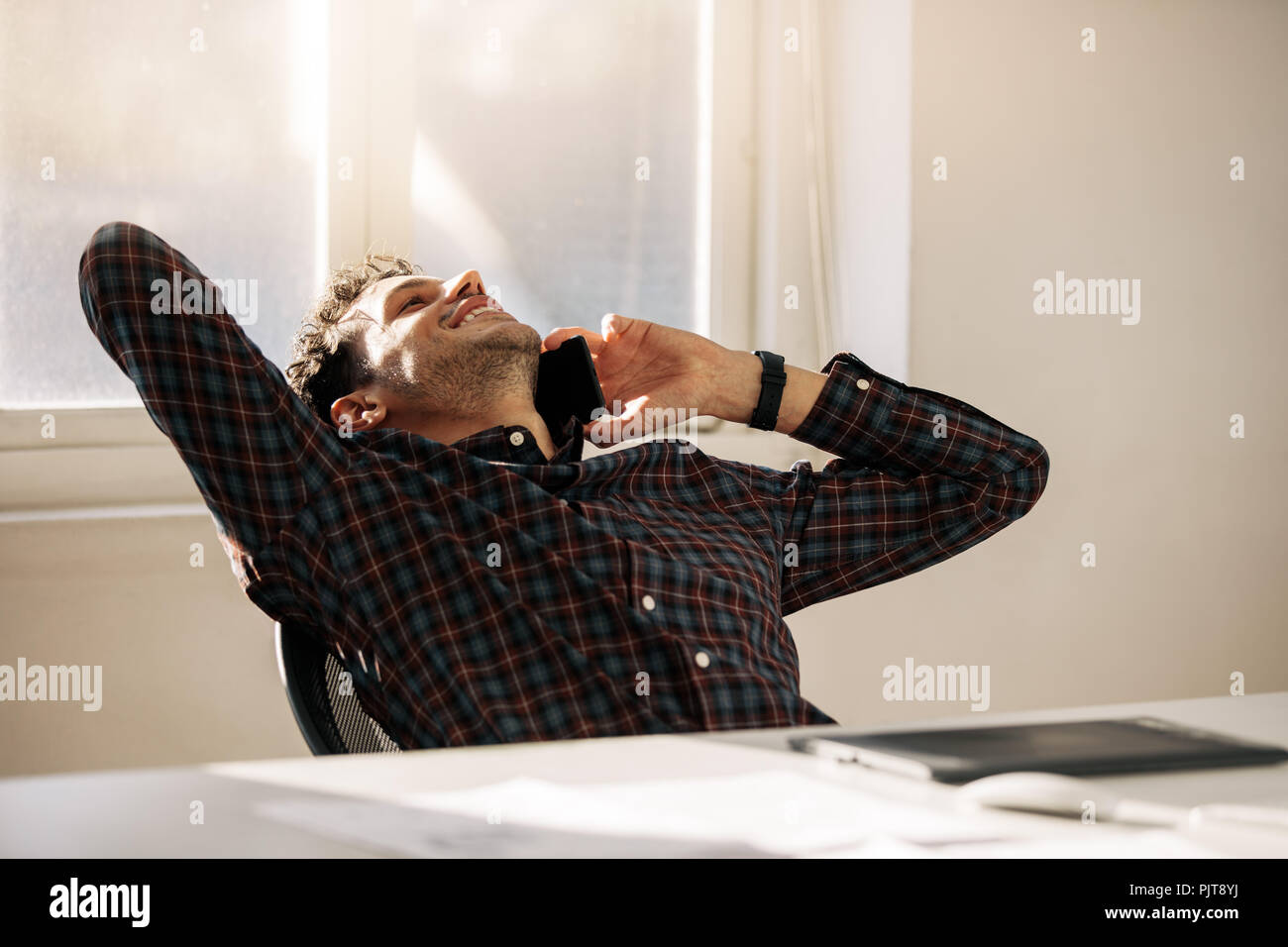 Entrepreneur relaxing back on his chair and talking on cell phone ...