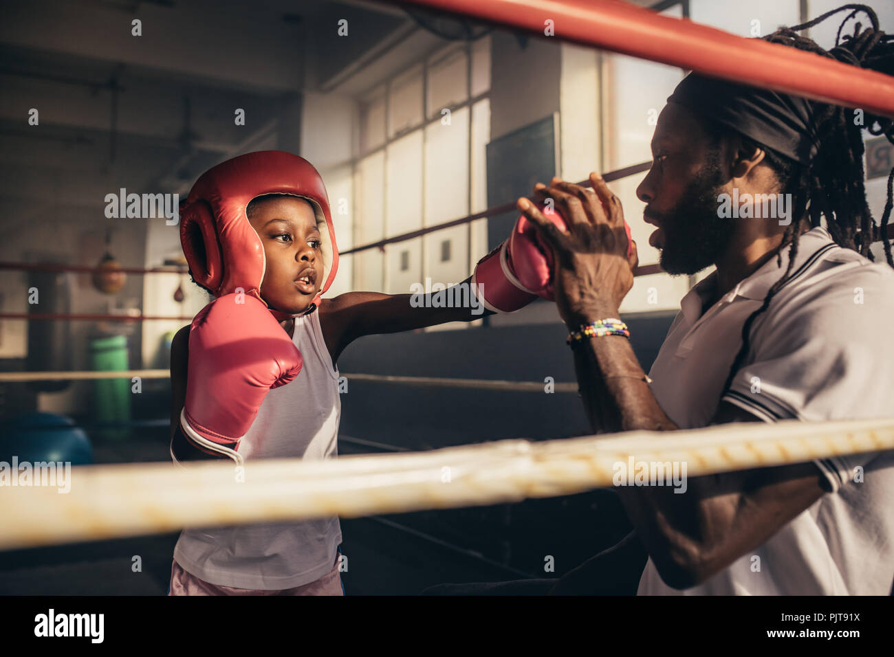Kid wearing boxing gloves and headgear hitting punches on hands of his ...