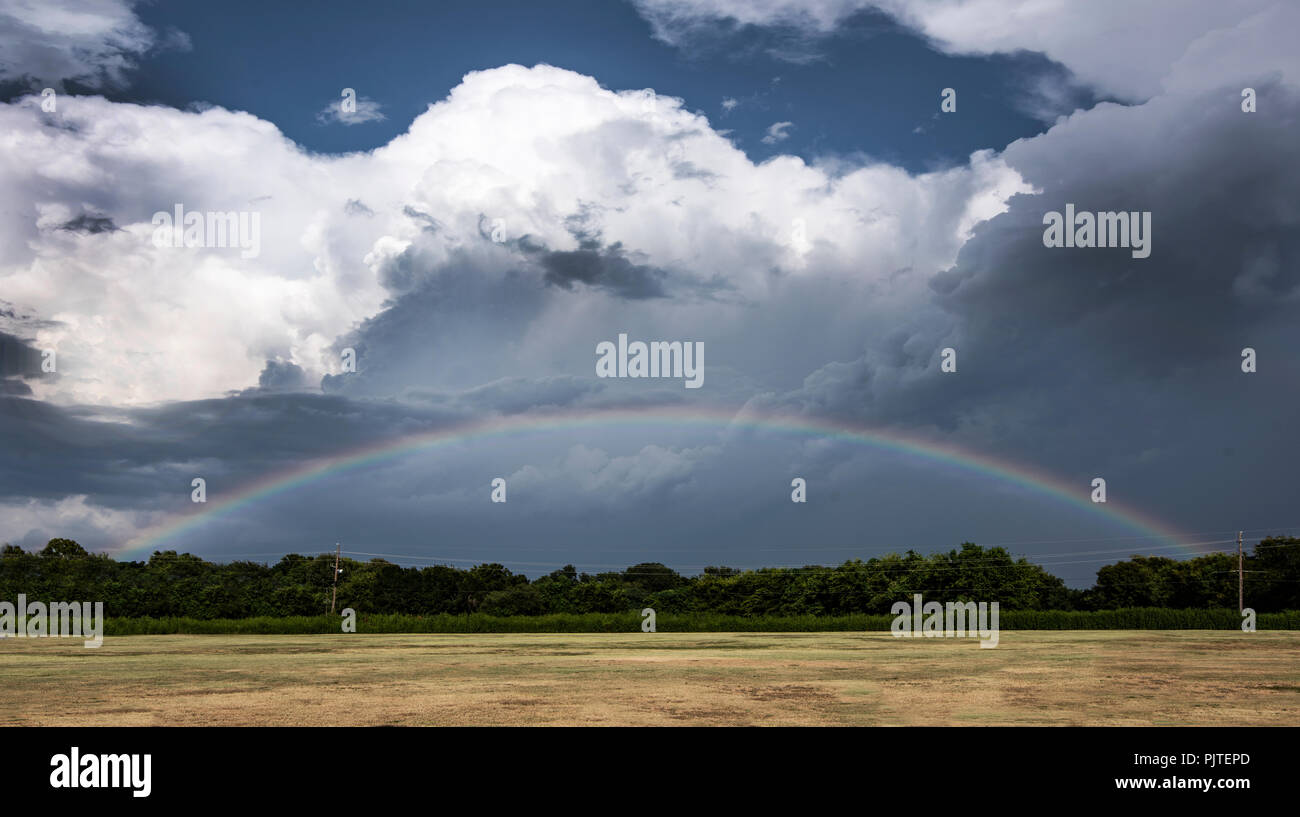 A rainbow and a few white clouds shine in striking contrast with dark ...