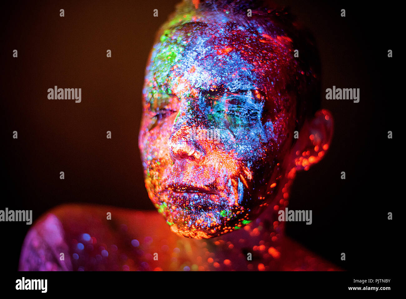 Studio portrait of a young woman covered in coloured powder, glowing ...
