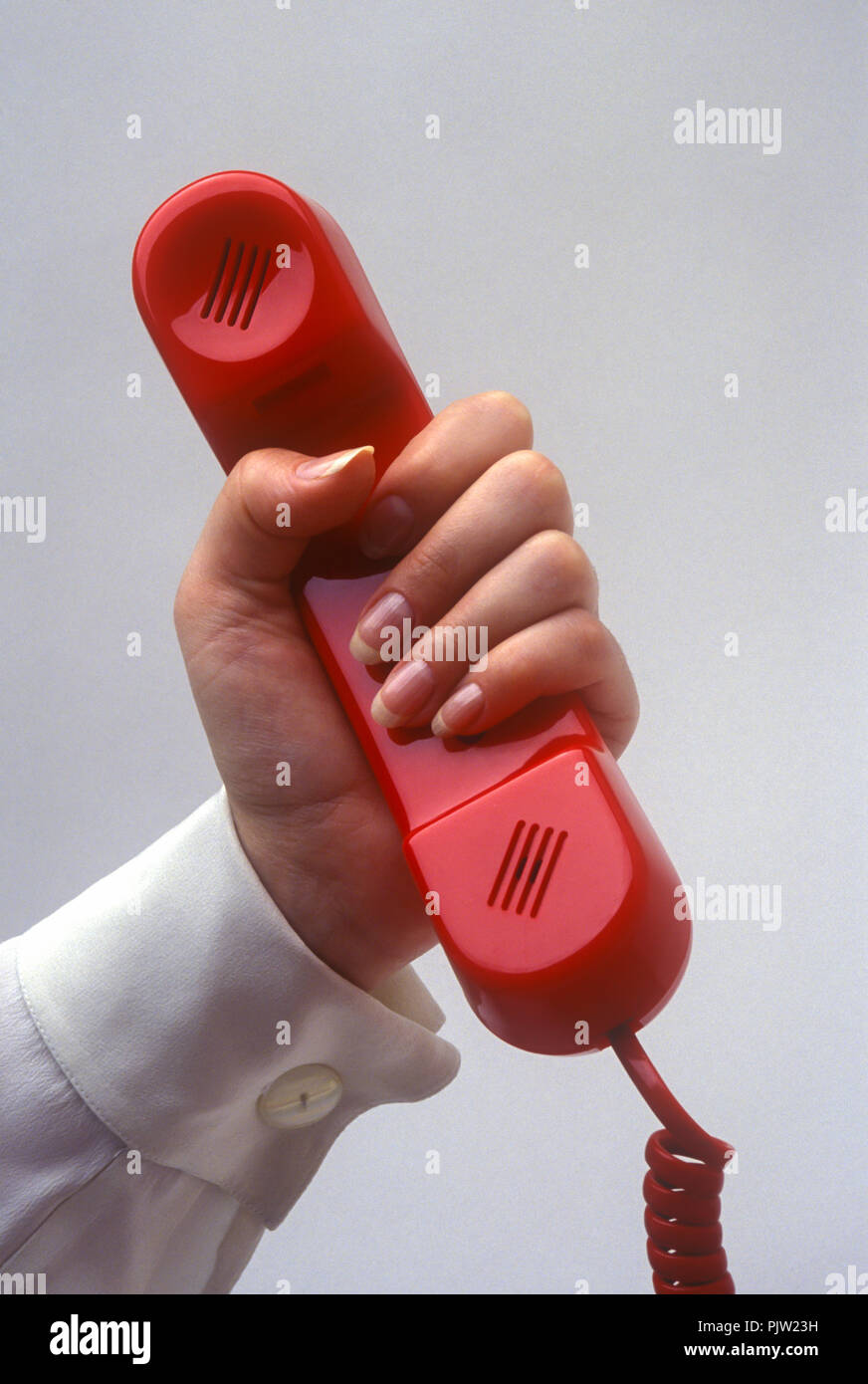 1991 HISTORICAL WOMANS HAND HOLDING UP RED LANDLINE TELEPHONE ON PLAIN ...