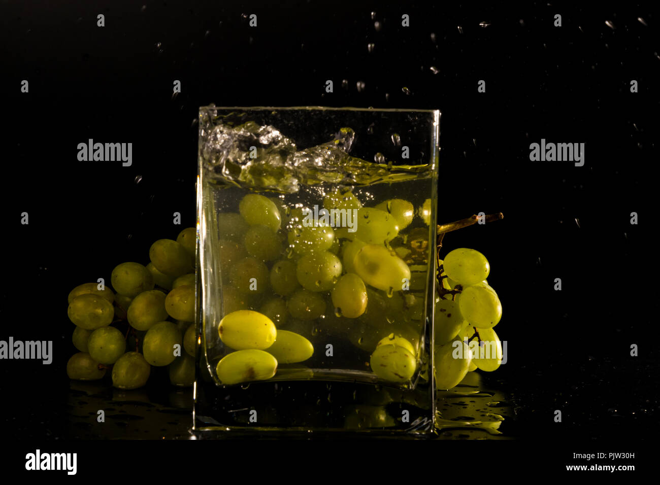 a bunch of grapes on a black background. jar of water splash from ...
