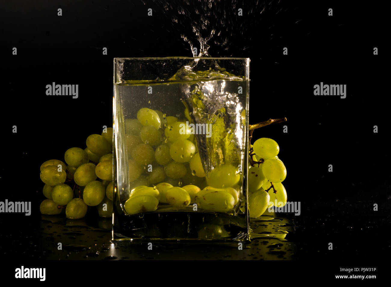 a bunch of grapes on a black background. jar of water splash from ...