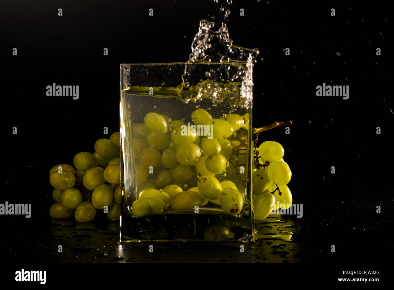 a bunch of grapes on a black background. jar of water splash from ...