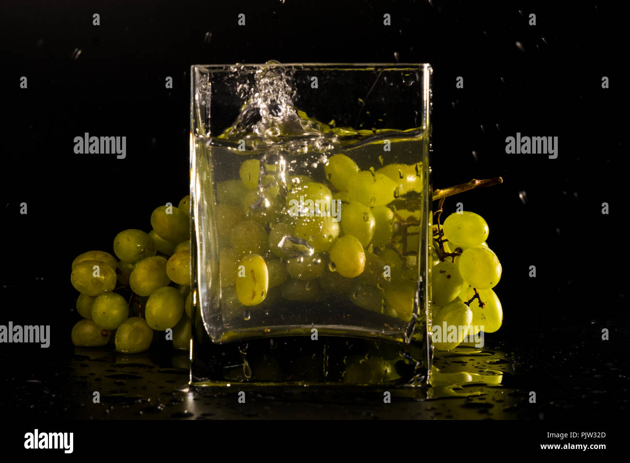 a bunch of grapes on a black background. jar of water splash from ...