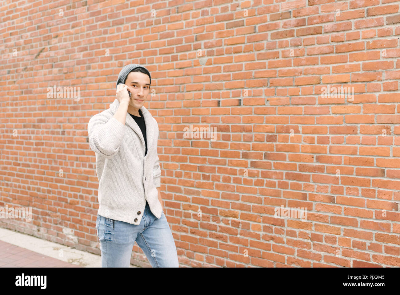 Young man talking on phone while walking along brick wall, Vancouver ...