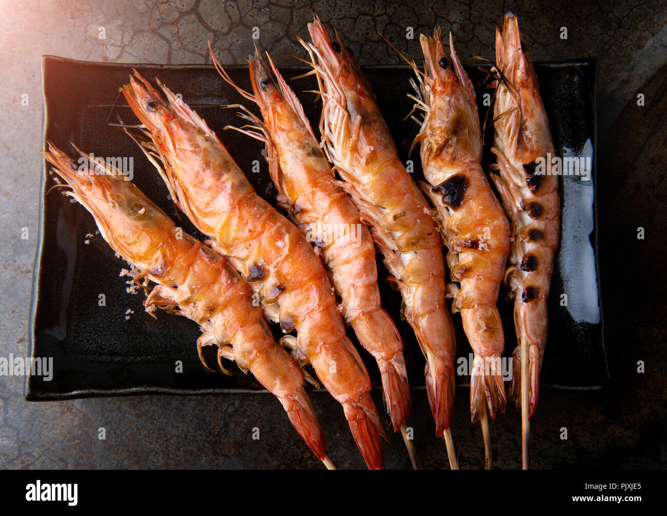 Skewer grilled shrimp with charcoal flaming fire serve in black dish ...