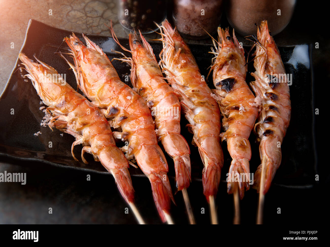 Skewer grilled shrimp with charcoal flaming fire serve in black dish ...