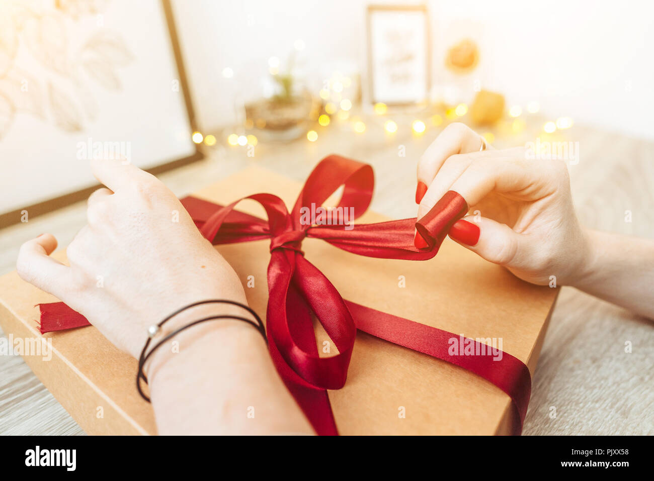 Woman wrapping present in paper with red ribbon Stock Photo - Alamy