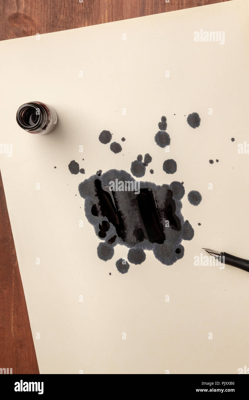 An overhead photo of an ink well with drops of ink and a nib pen, with ...