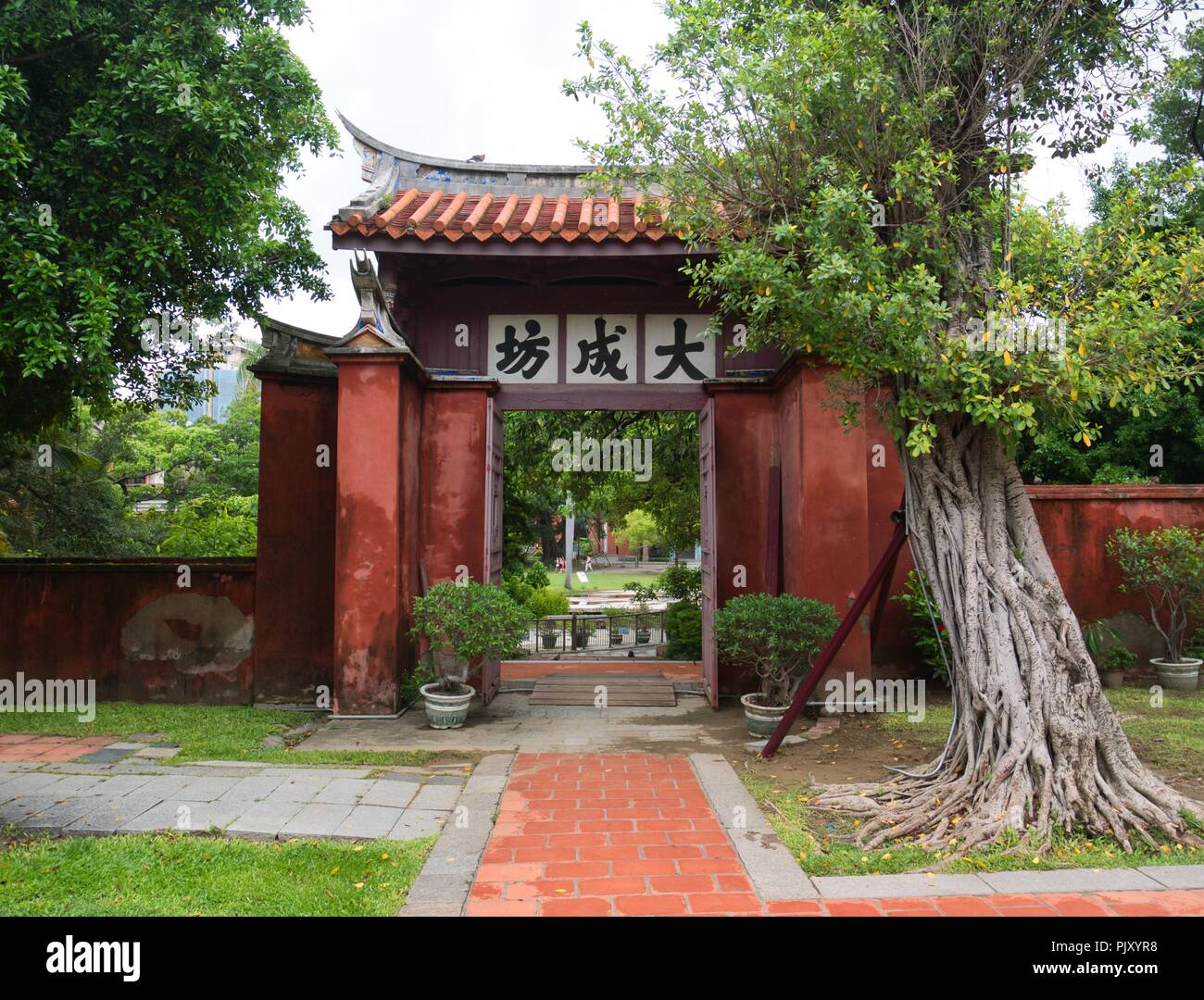 Traditional chinese entrance to a park. Old tree und red stone paved ...