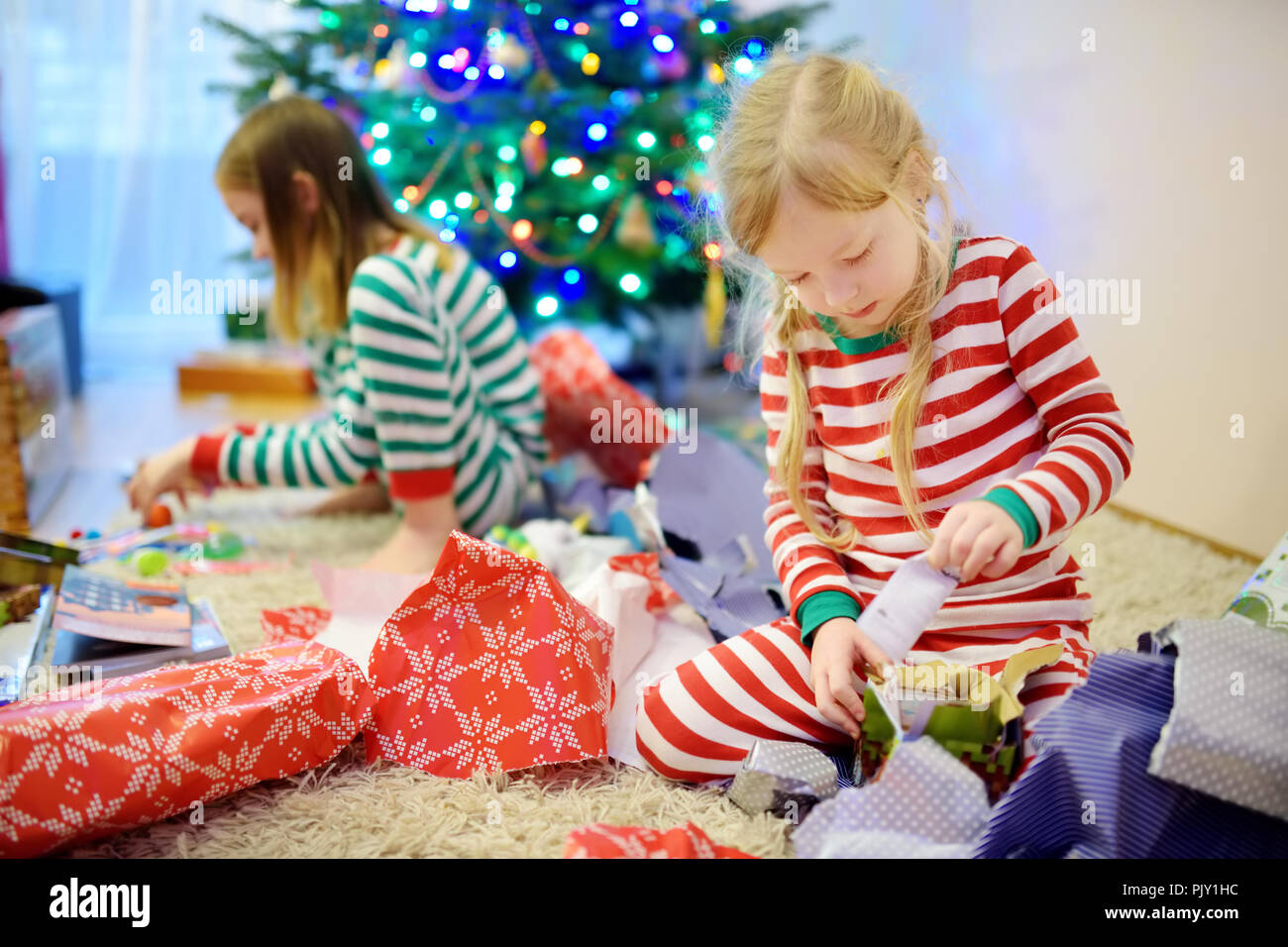 Adorable little sisters wearing Christmas pajamas opening gifts and ...