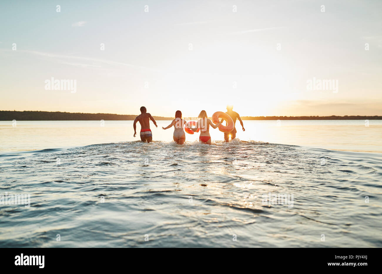 Rearview of a diverse group of young friends in swimsuits running into ...