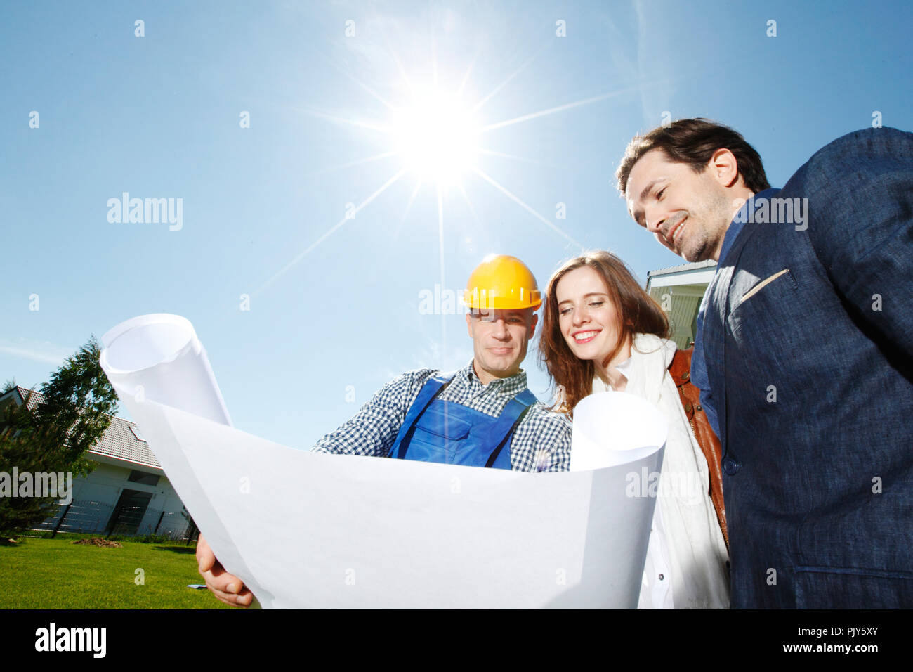 Worker shows house design plans to a young couple at construction site ...