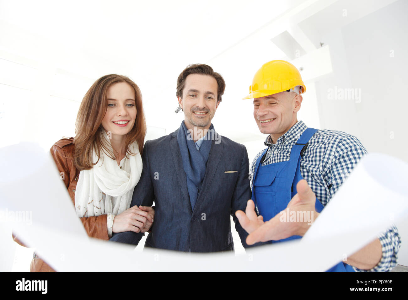 Worker shows house design plans to a young couple at construction site ...