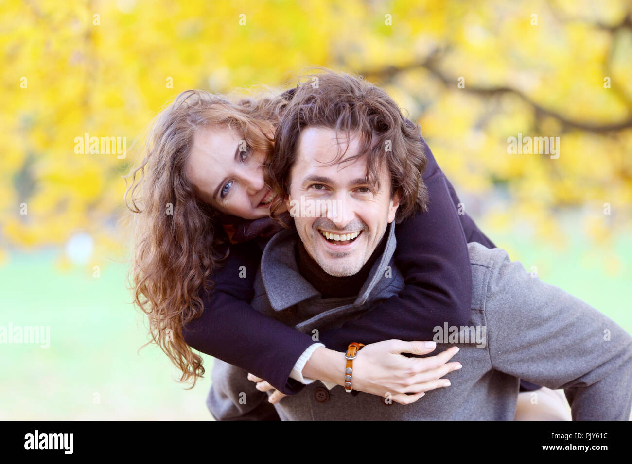 Smiling mid adult couple hug in autumn forest of yellow maple trees ...