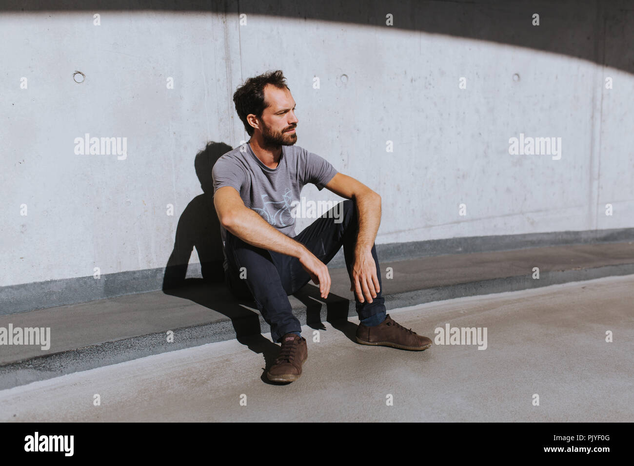 thoughtful caucasian man leaning against a concrete wall looking sad ...