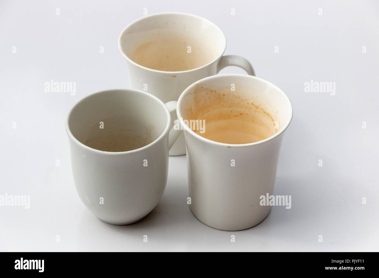 A Close up side view of three dirty white coffee mugs in a group on a ...