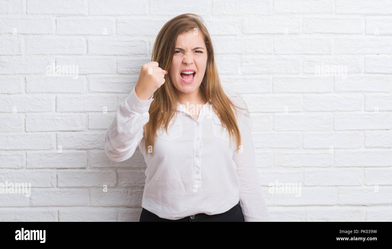 Young adult business woman over white brick wall annoyed and frustrated ...