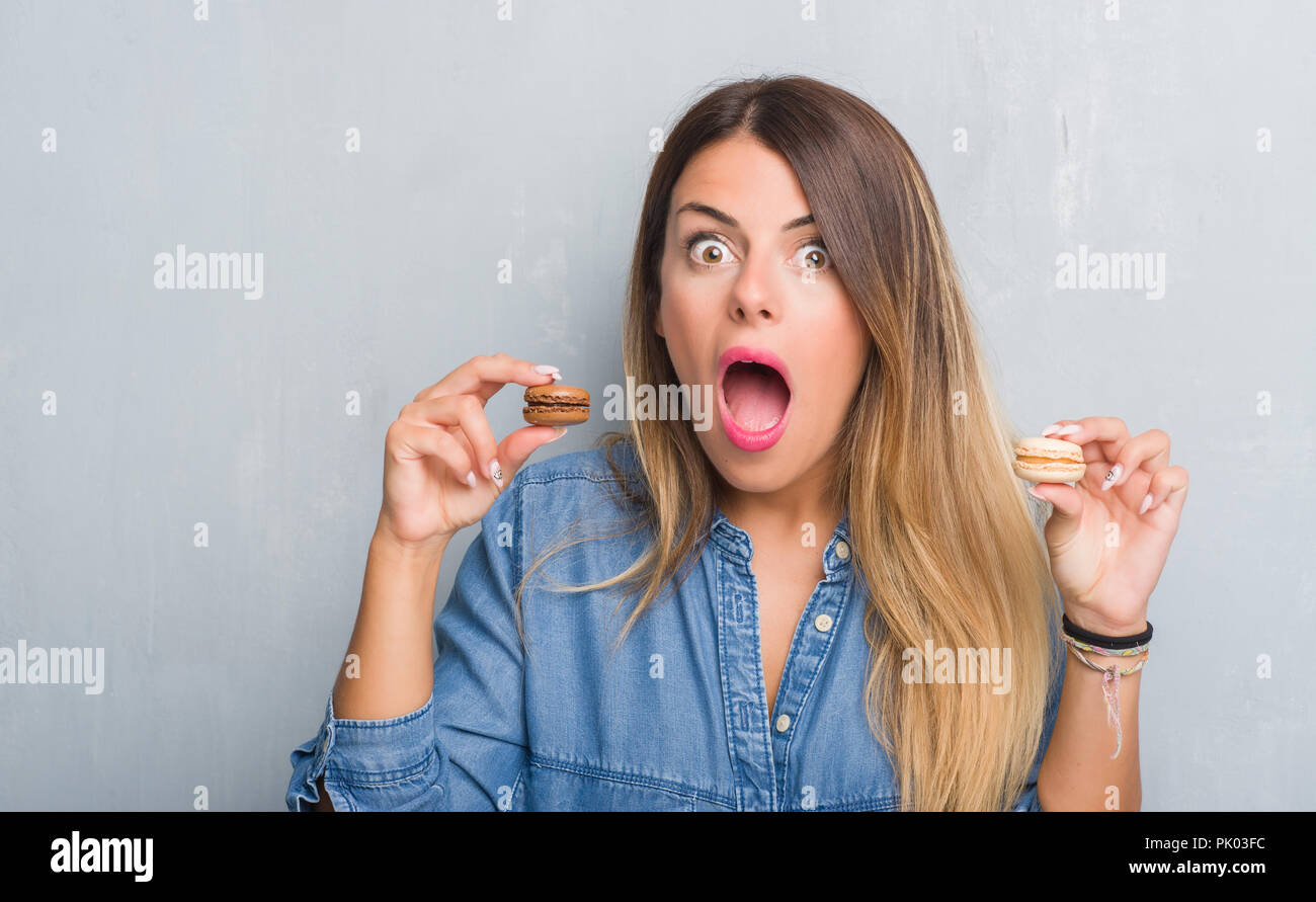 Young adult woman over grey grunge wall eating chocolate macarons ...